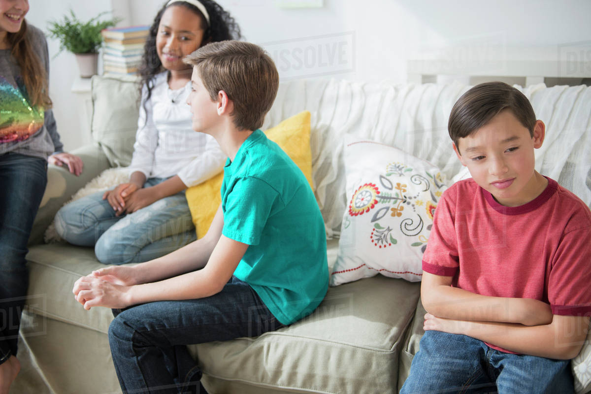 Pouting boy ignoring friends in living room - Stock Photo - Dissolve