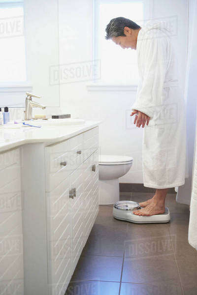 Asian man standing on bathroom scale - Stock Photo - Dissolve