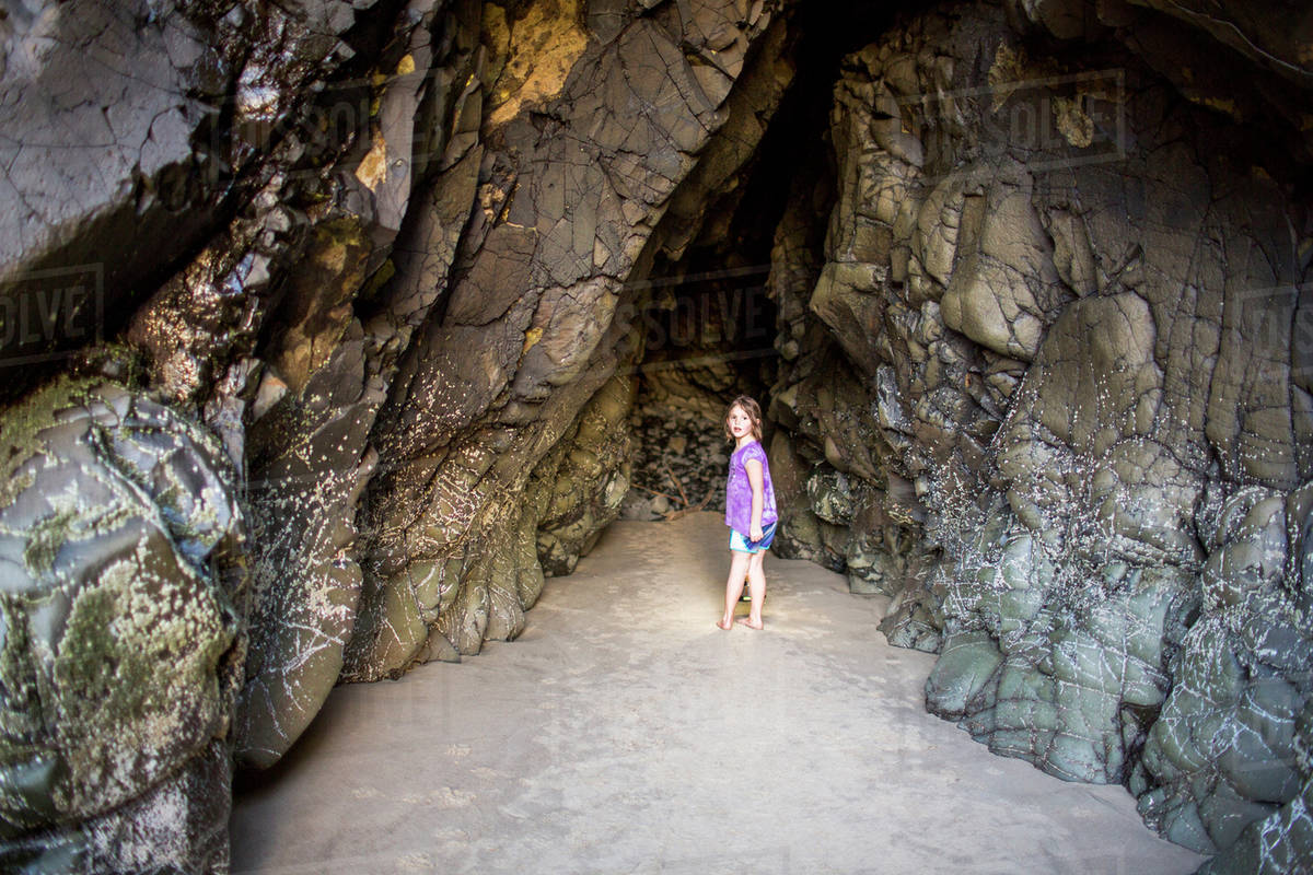 Caucasian girl exploring cave at beach - Stock Photo - Dissolve