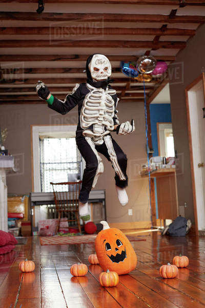 Black boy jumping over pumpkin in skeleton Halloween costume - Royalty ...