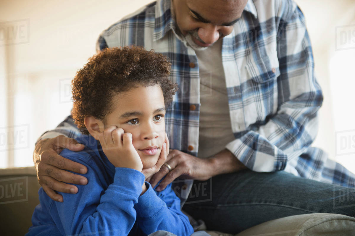 Mixed race grandfather comforting grandson on sofa - Stock Photo - Dissolve