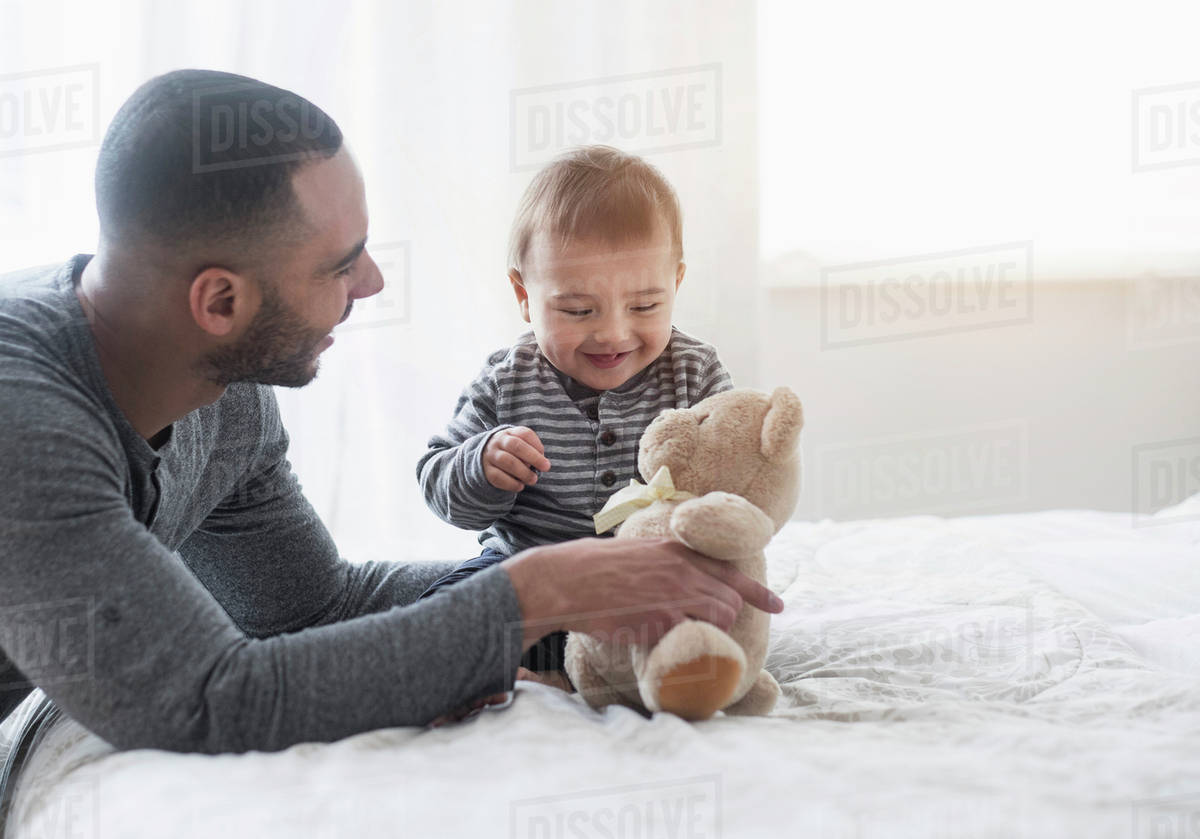 Smiling father playing with baby son on bed - Stock Photo - Dissolve