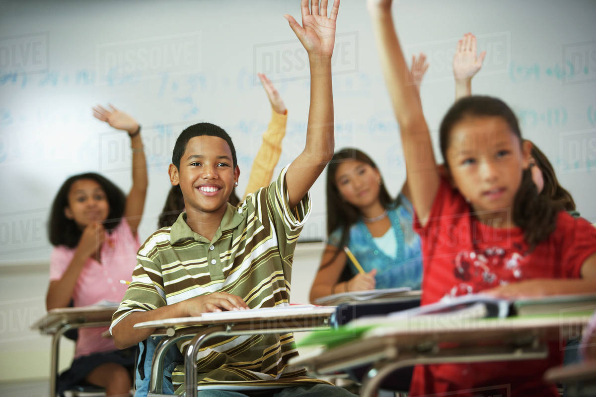 Multi-ethnic students raising hands in class - Stock Photo - Dissolve