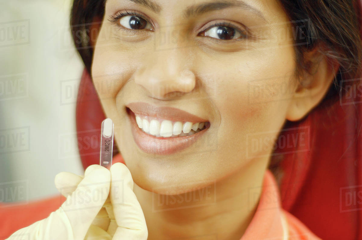 Tooth color sample being held up next to Indian woman's teeth - Stock ...