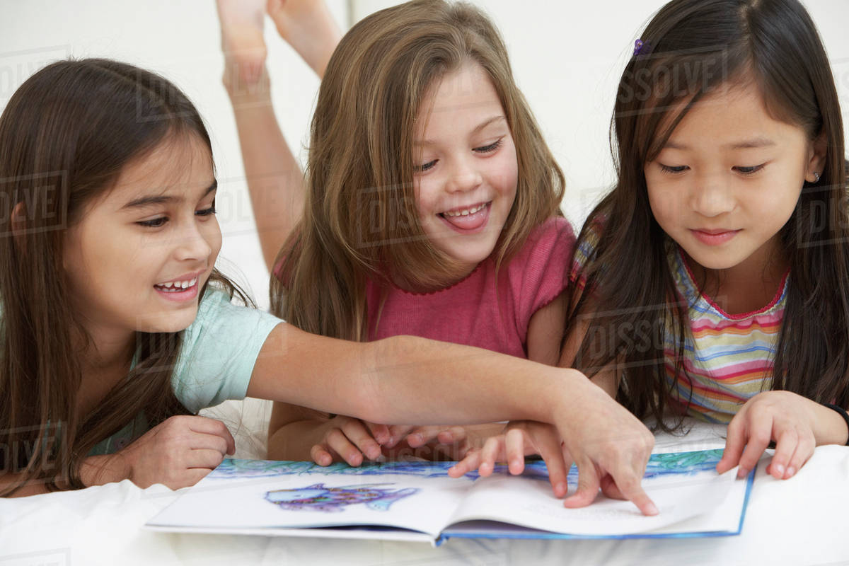 Three young girls reading book - Stock Photo - Dissolve
