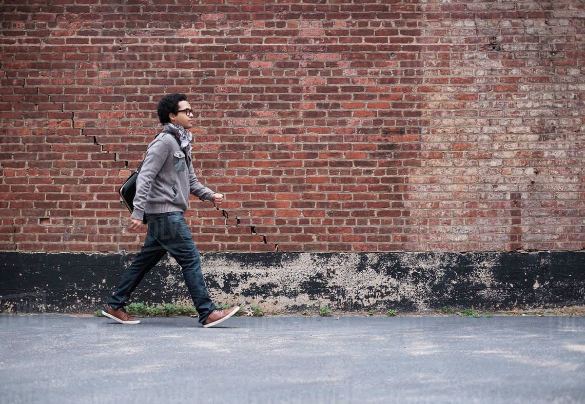 Mixed race man walking near brick wall - Royalty-free Stock Photo ...