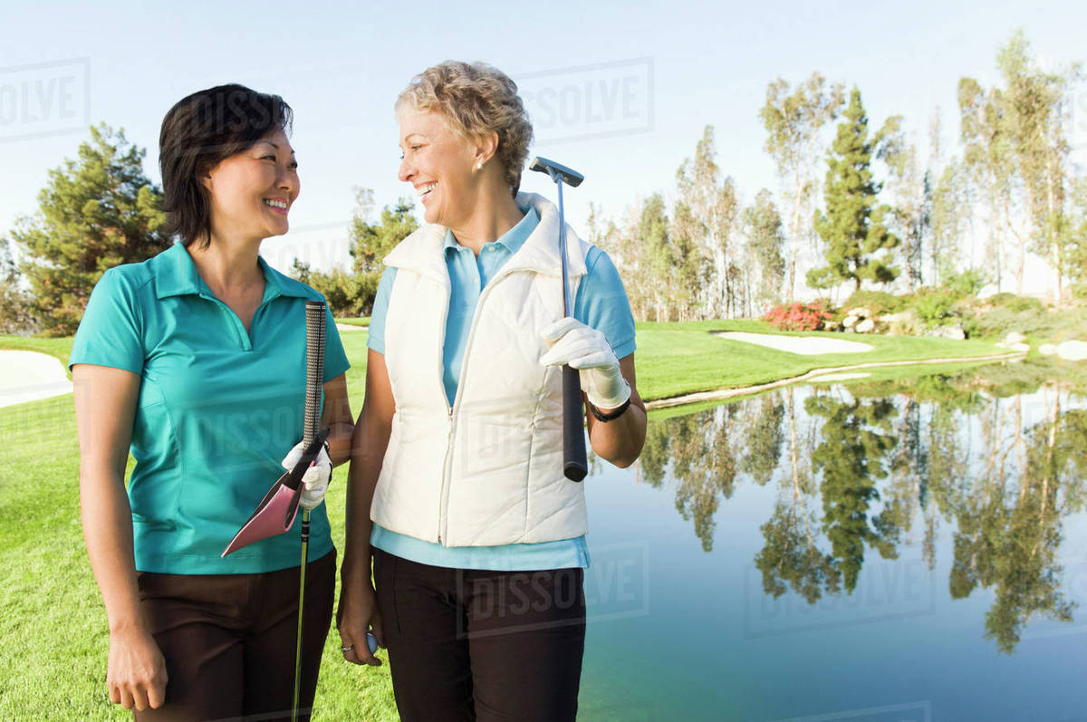 Women laughing on golf course near water hazard - Stock Photo - Dissolve