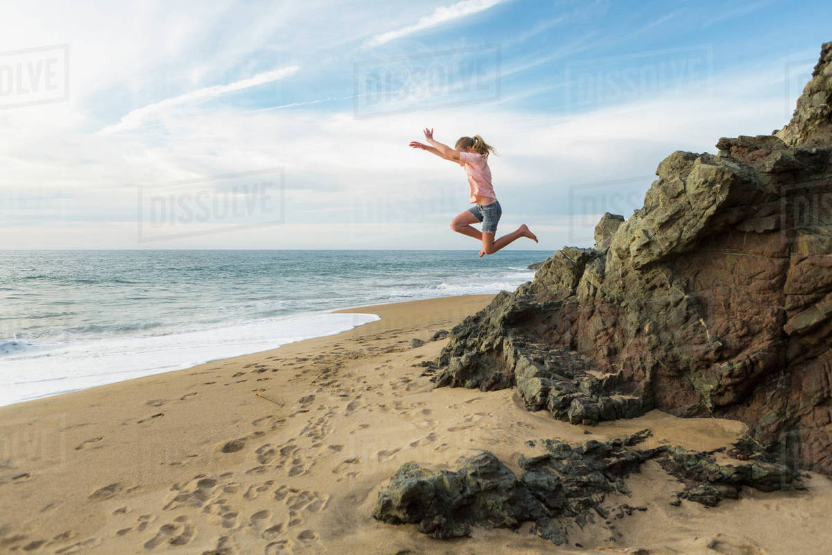 Caucasian girl jumping off rocks at beach - Royalty-free Stock Photo ...