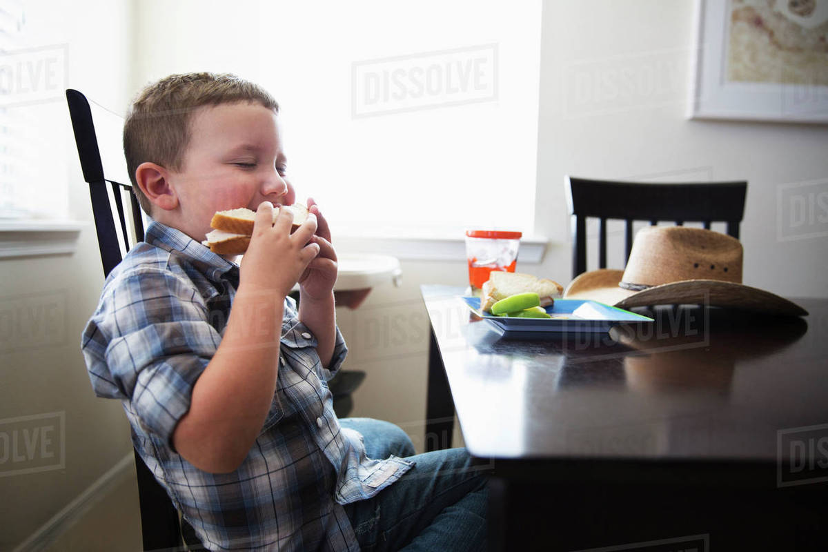 Caucasian boy eating sandwich at table - Stock Photo - Dissolve