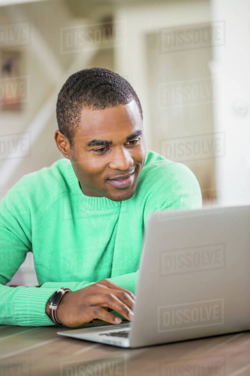 Black man sitting at table using laptop - Royalty-free Stock Photo ...