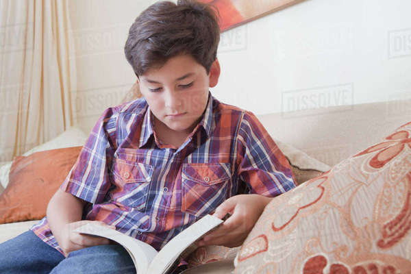 Hispanic boy reading book on sofa - Stock Photo - Dissolve