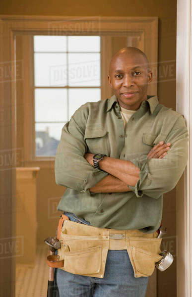 African man wearing tool belt with arms crossed - Stock Photo - Dissolve