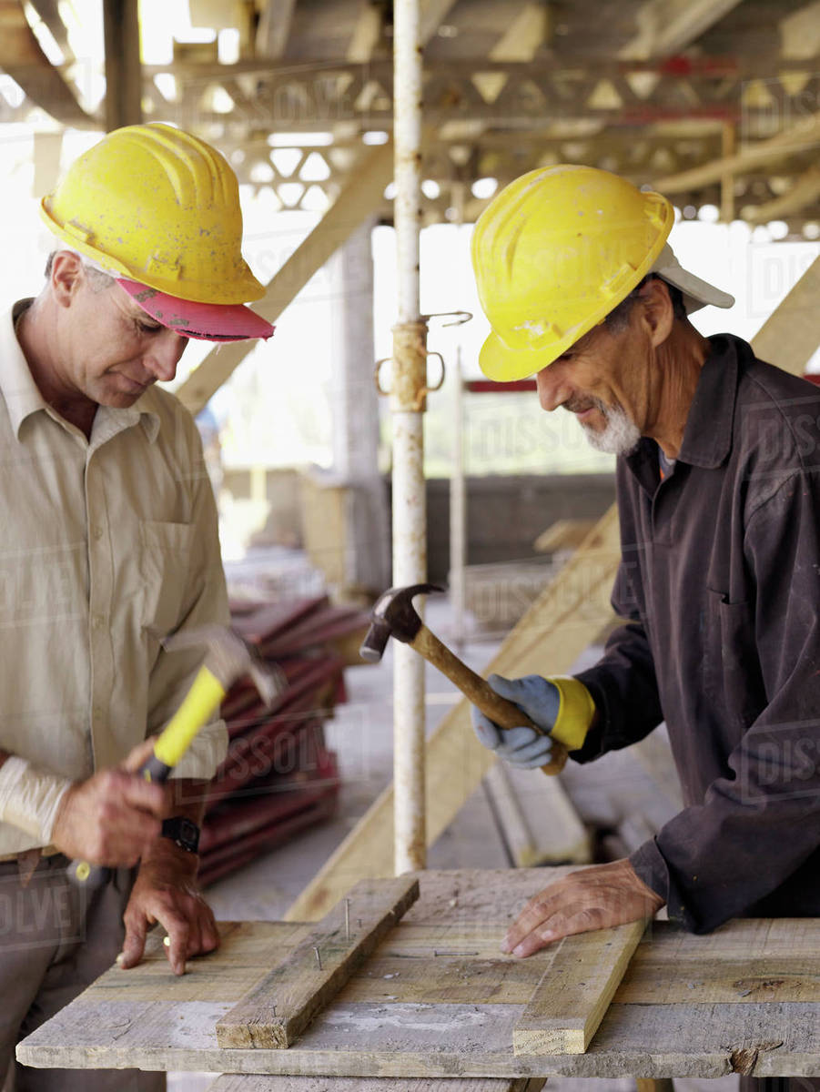 Hispanic workers using hammers at construction site - Royalty-free ...