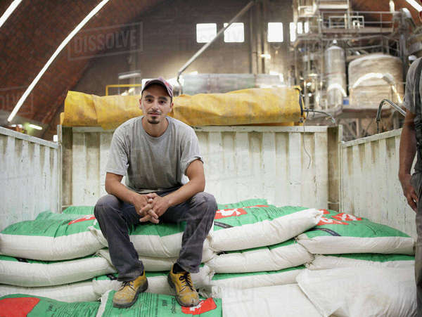 Hispanic worker sitting on bag in factory - Stock Photo - Dissolve
