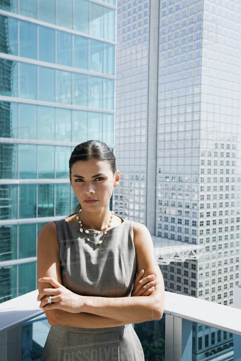 Serious Hispanic Woman Standing On Urban Balcony With Arms Crossed