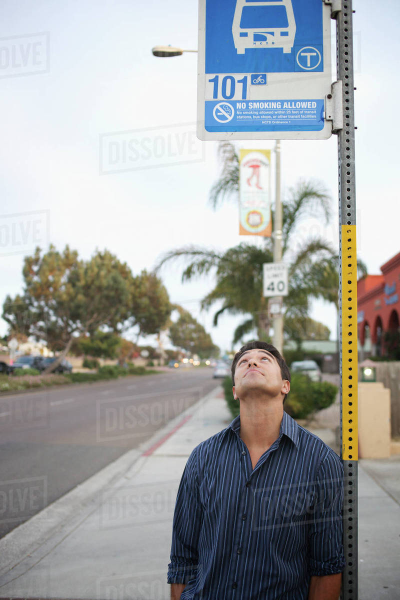 Mixed race man looking at bus stop sign - Stock Photo - Dissolve