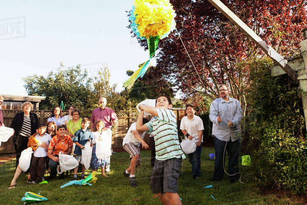 Hispanic family breaking pinata in backyard - Stock Photo - Dissolve
