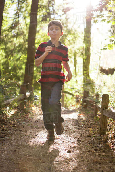 Caucasian boy running on path in forest - Stock Photo - Dissolve
