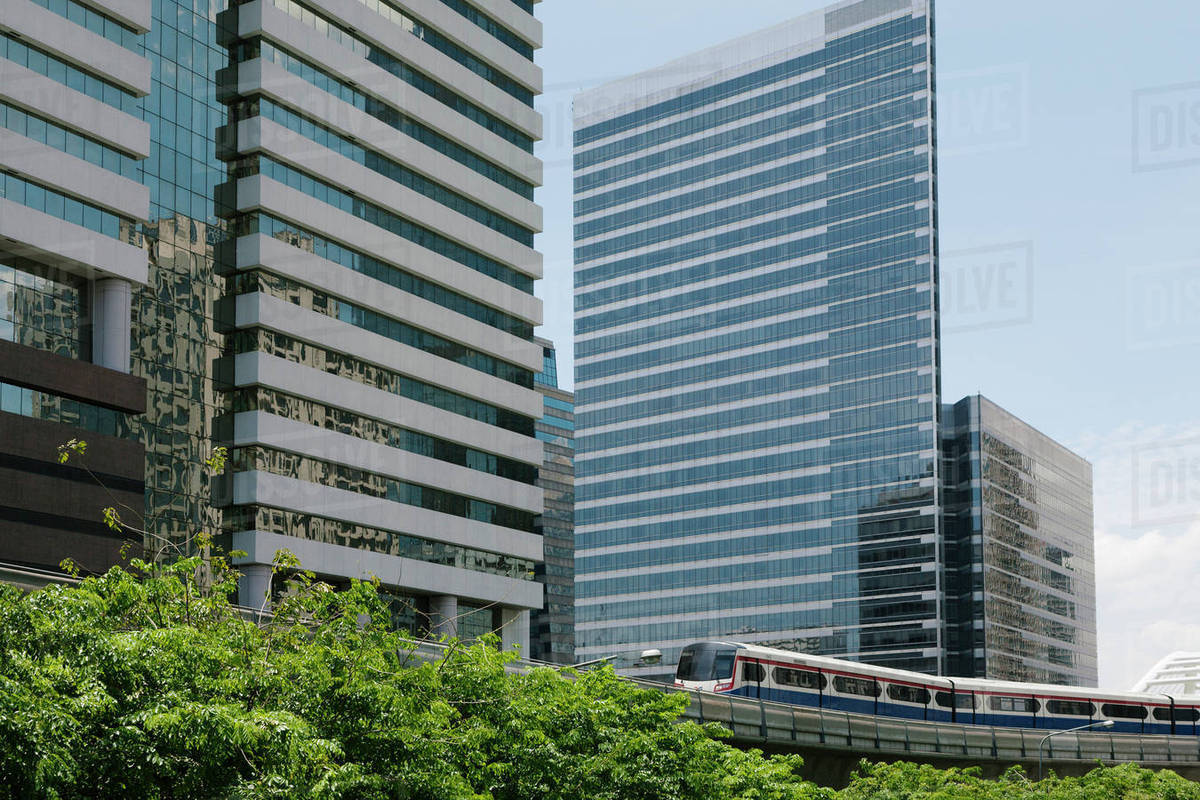 A mass transit train on an elevated track passes modern building ...