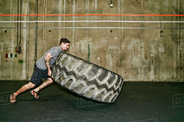Caucasian man lifting large tire in gym - Stock Photo - Dissolve