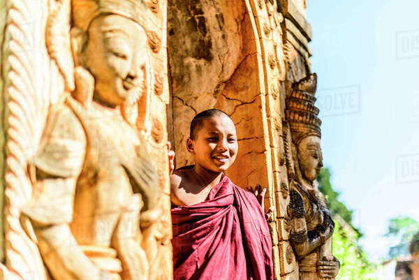 Asian monk-in-training peering around carved temple walls - Royalty ...