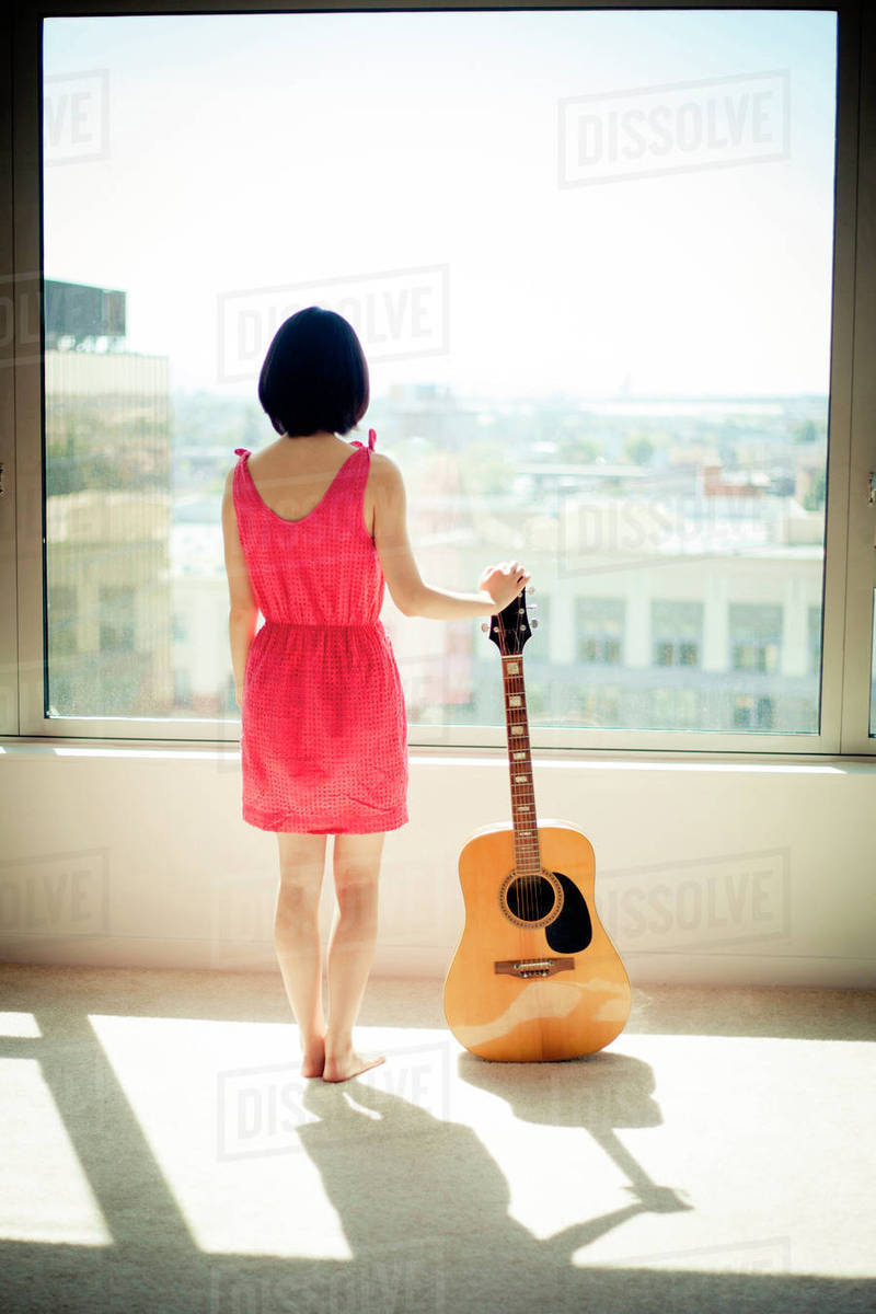 Asian woman holding guitar in window - Stock Photo - Dissolve