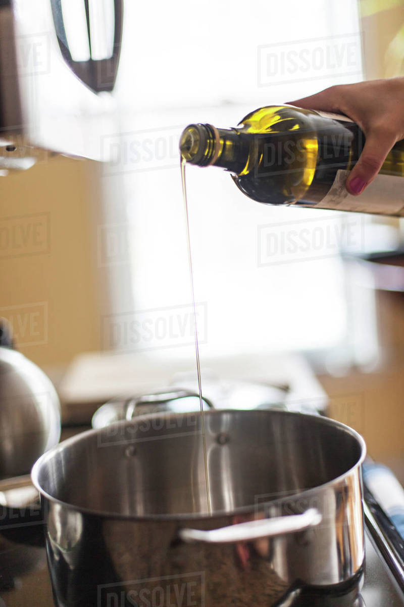 Close up of woman pouring olive oil into pot - Stock Photo - Dissolve