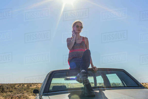 Caucasian woman sitting on roof of car in desert - Stock Photo - Dissolve
