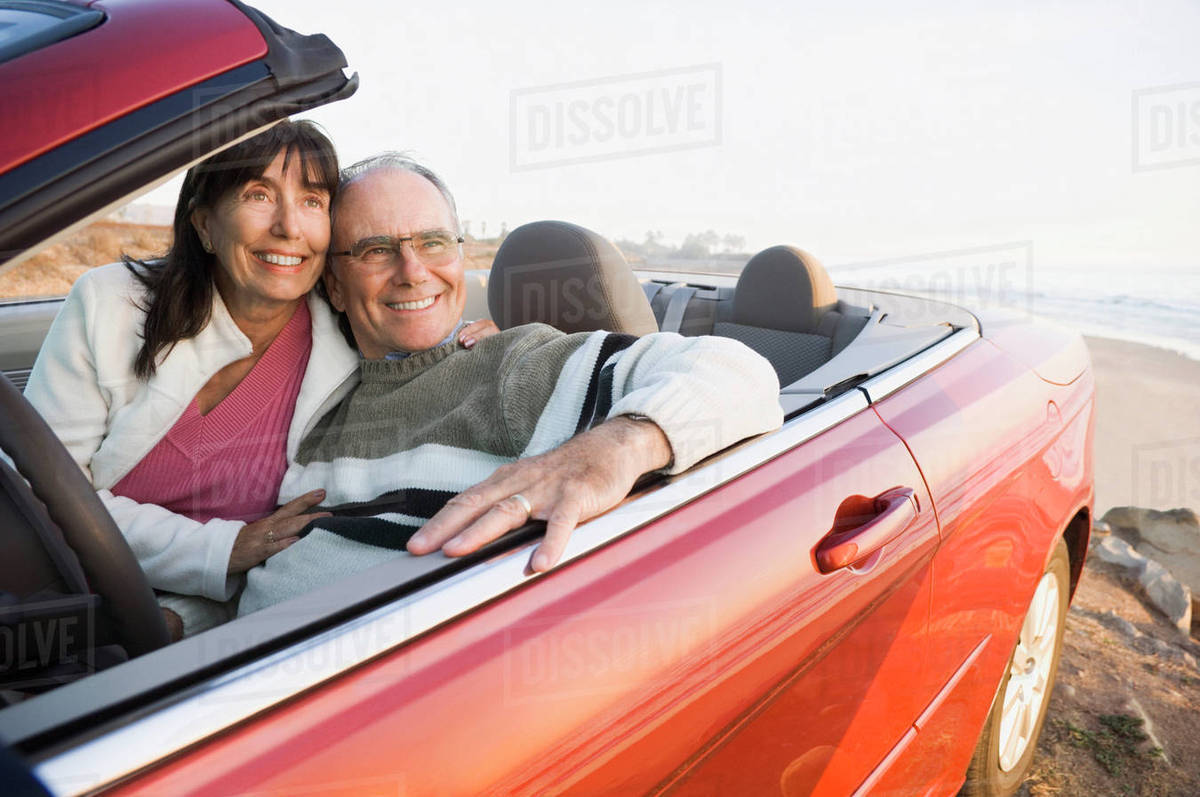 Older couple driving convertible on beach - Stock Photo - Dissolve