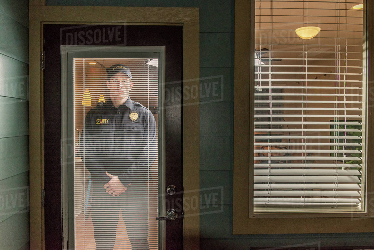 Caucasian security officer standing behind door with blinds - Royalty ...