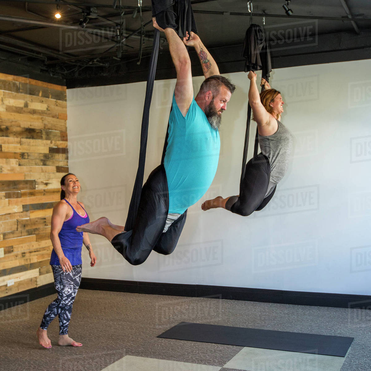 Instructor watching students performing yoga hanging from silks - Stock ...