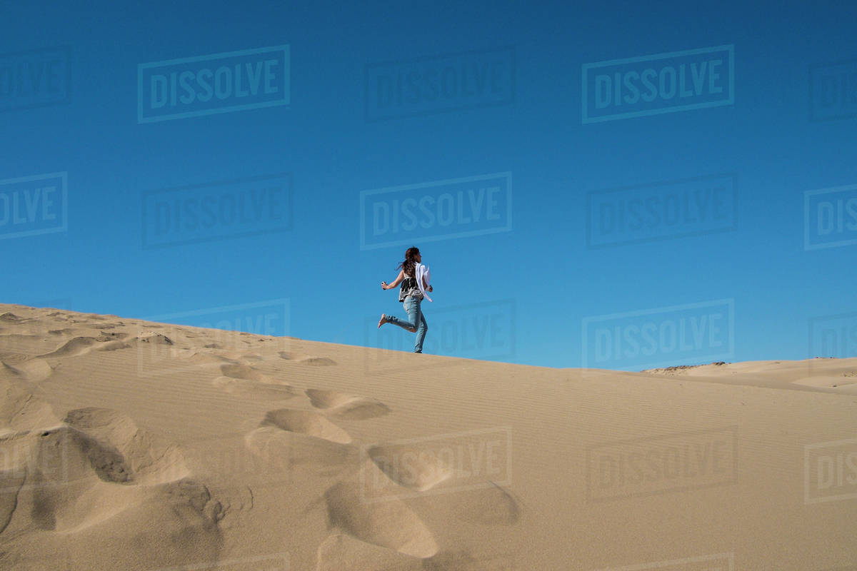 Caucasian woman running on sand dune - Royalty-free Stock Photo | Dissolve