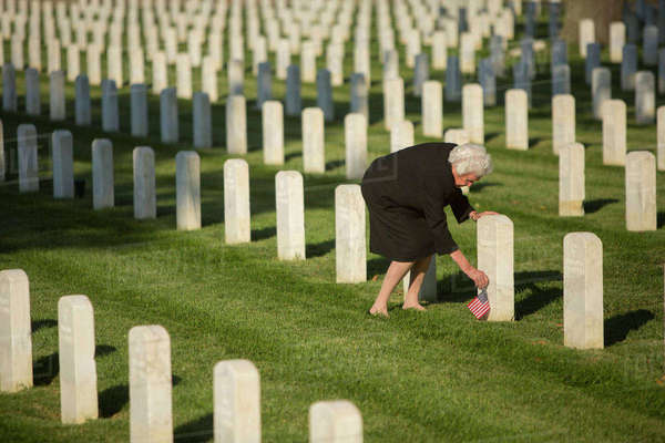 Caucasian widow placing American flag at cemetery gravestone - Royalty ...