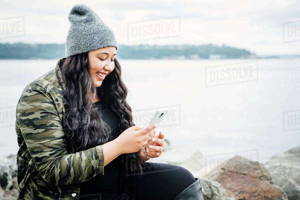 Smiling Mixed Race woman texting on cell phone near ocean - Royalty ...