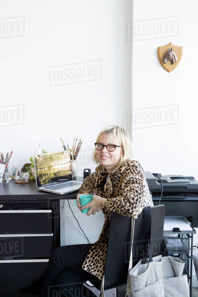Caucasian woman drinking coffee at desk with laptop - Royalty-free ...