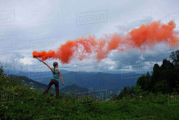 Caucasian girl holding orange smoke flare on mountain range - Royalty ...