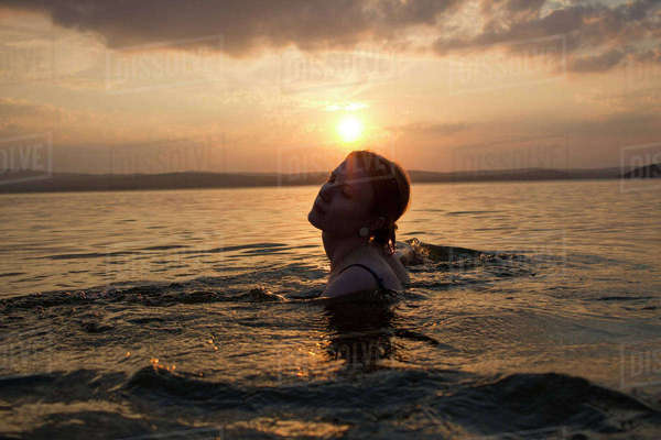 Woman swimming in lake at sunset - Royalty-free Stock Photo | Dissolve