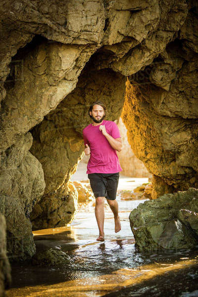Caucasian man running under rock formation at beach - Stock Photo ...