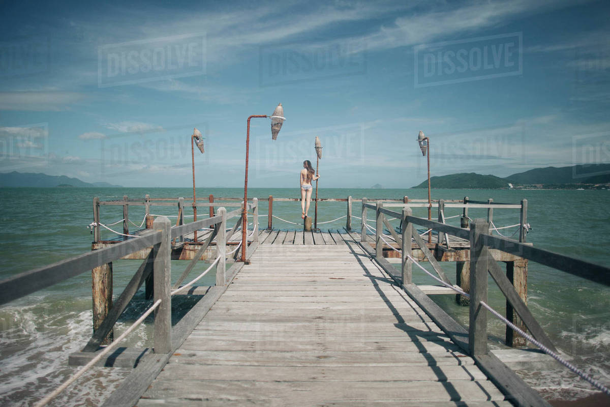 Woman wearing bikini standing on railing on dock - Stock Photo - Dissolve