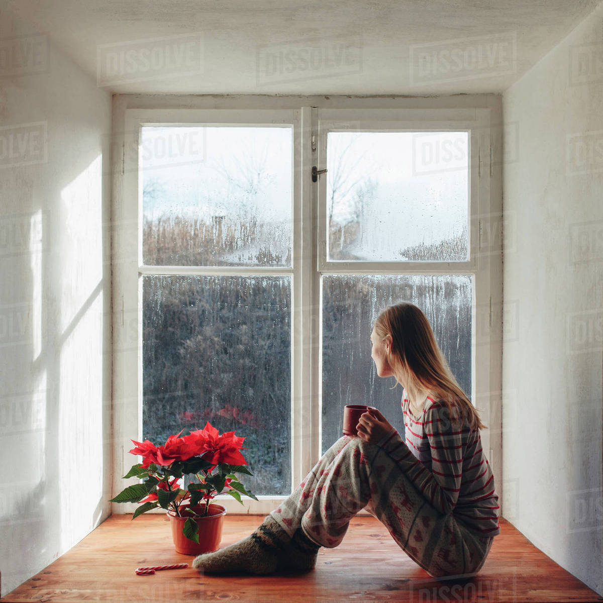 Caucasian woman sitting in window sill drinking coffee in pajamas ...
