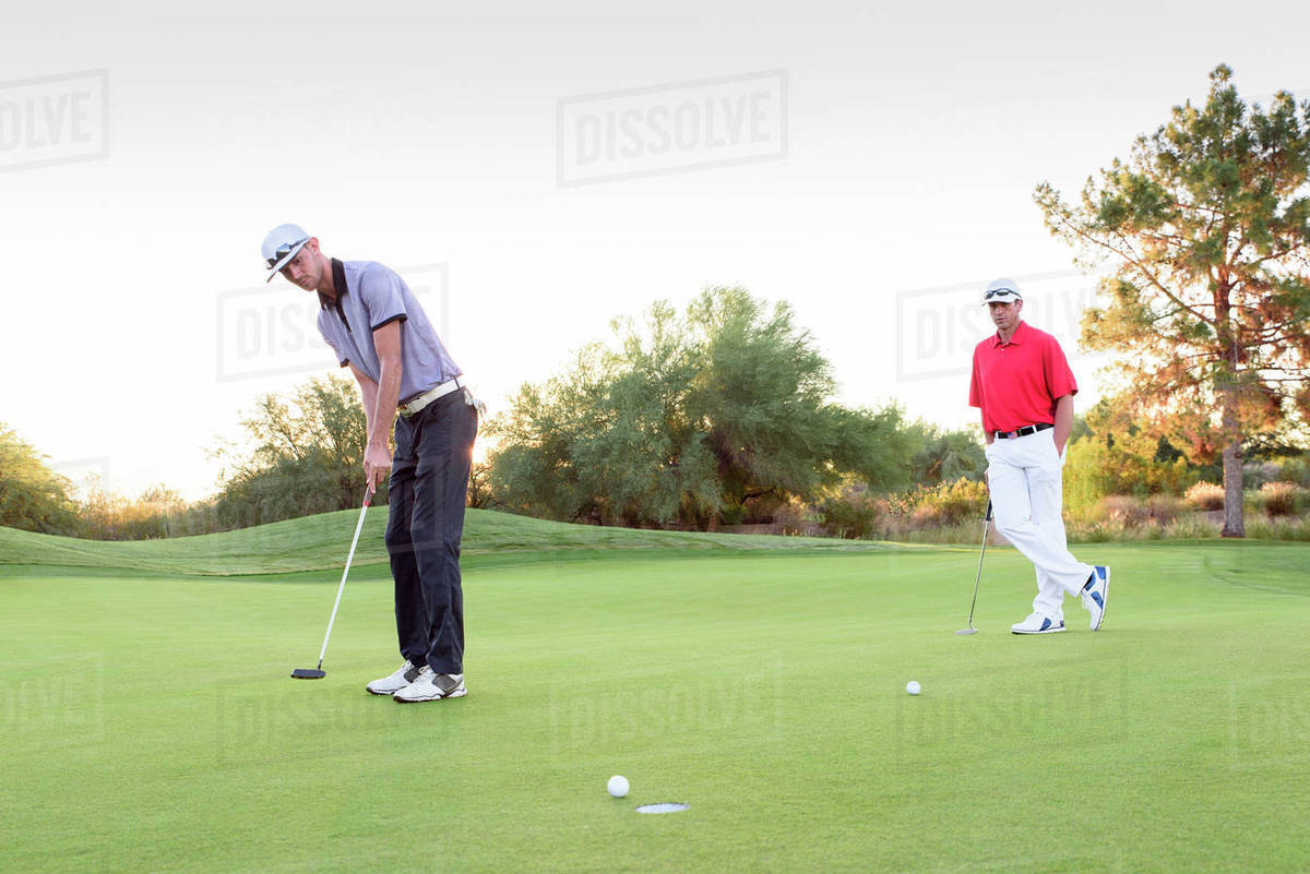 Man watching friend putting on golf course - Stock Photo - Dissolve