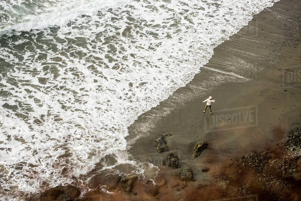 Distant Caucasian woman throwing stone on ocean beach - Royalty-free ...