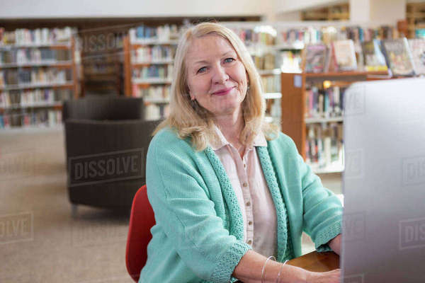 Smiling Caucasian woman using computer in library - Stock Photo - Dissolve