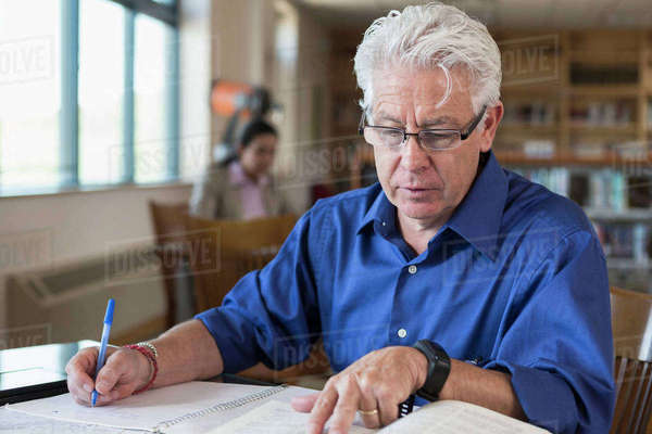 Hispanic man reading book and writing notes in library - Stock Photo ...
