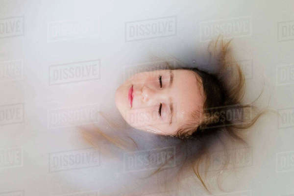 Face of Caucasian girl floating in bathtub - Stock Photo - Dissolve