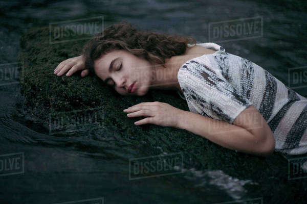 Caucasian girl laying face on a rock in ocean - Stock Photo - Dissolve