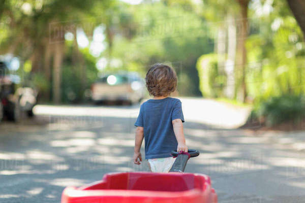 Caucasian boy pulling red wagon in street - Stock Photo - Dissolve