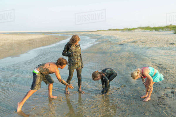 Caucasian brother and sisters covered in mud playing on beach - Royalty ...