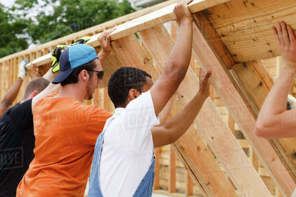 Volunteers lifting framed wall at construction site - Royalty-free ...