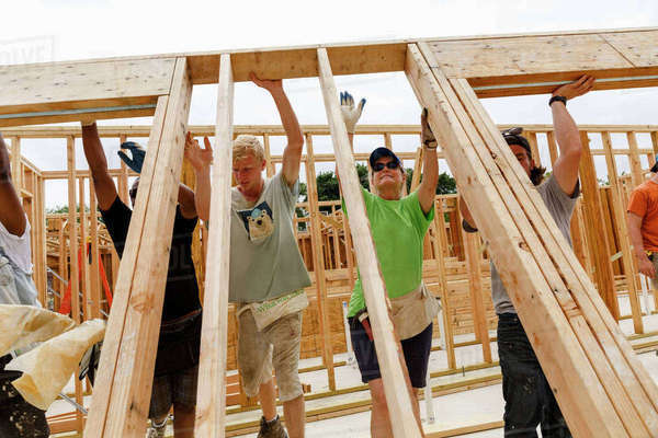 Volunteers lifting framed wall at construction site - Stock Photo ...
